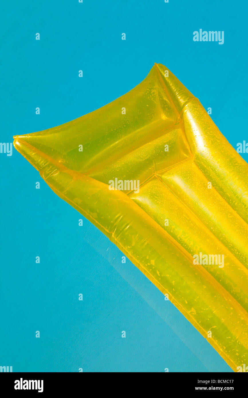 Yellow lilo inflatable air mat bed on bright blue clear water in sunny ...