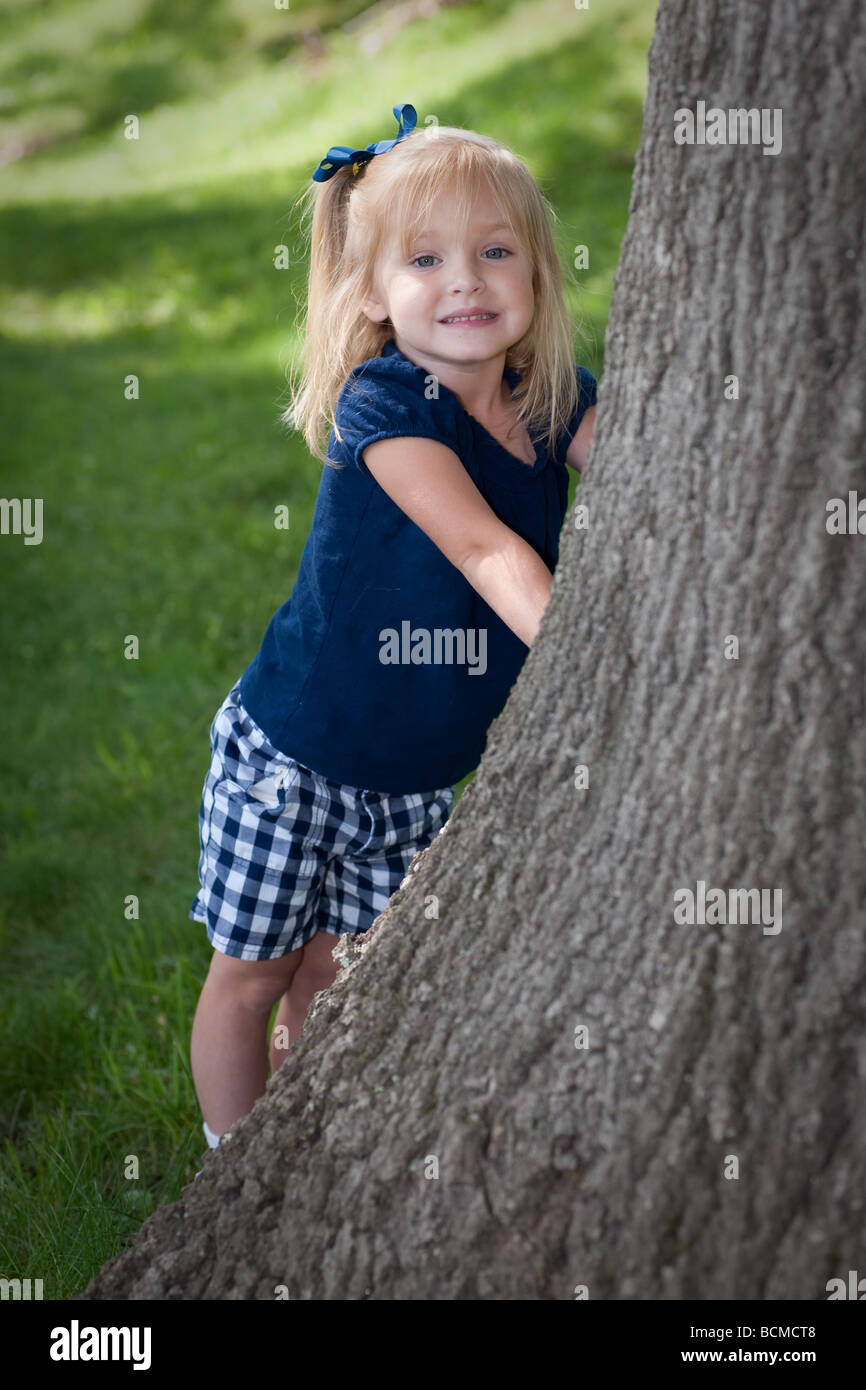 little girl smiling and standing behind tree Stock Photo - Alamy