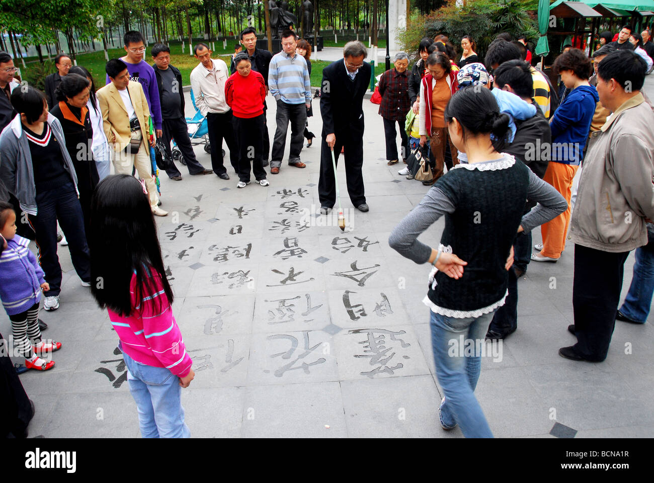Elerly Chinese man practicing calligraphy on the ground as crowds ...