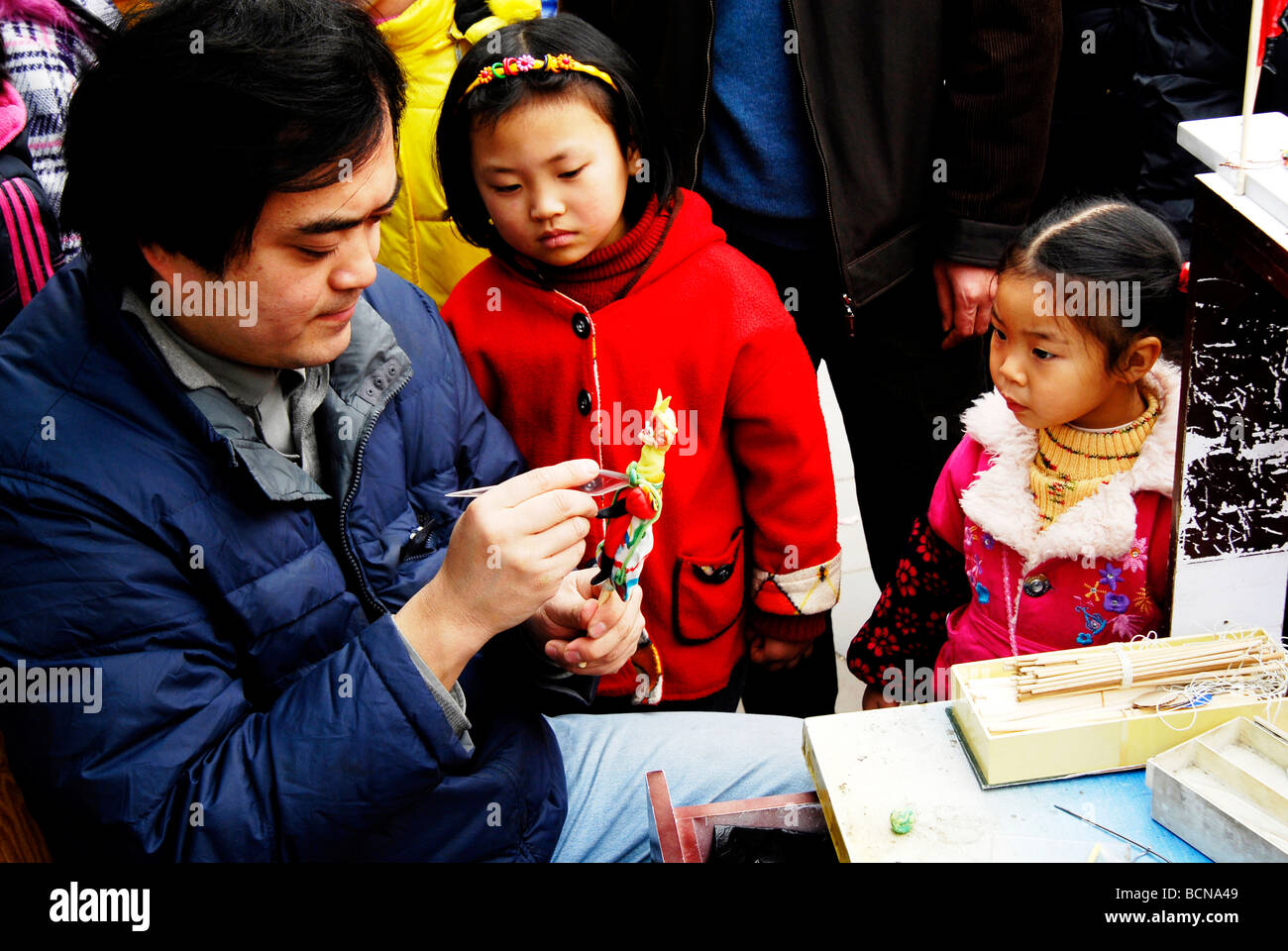 Street artist making flour doll as two young girls looking on, Chengdu ...