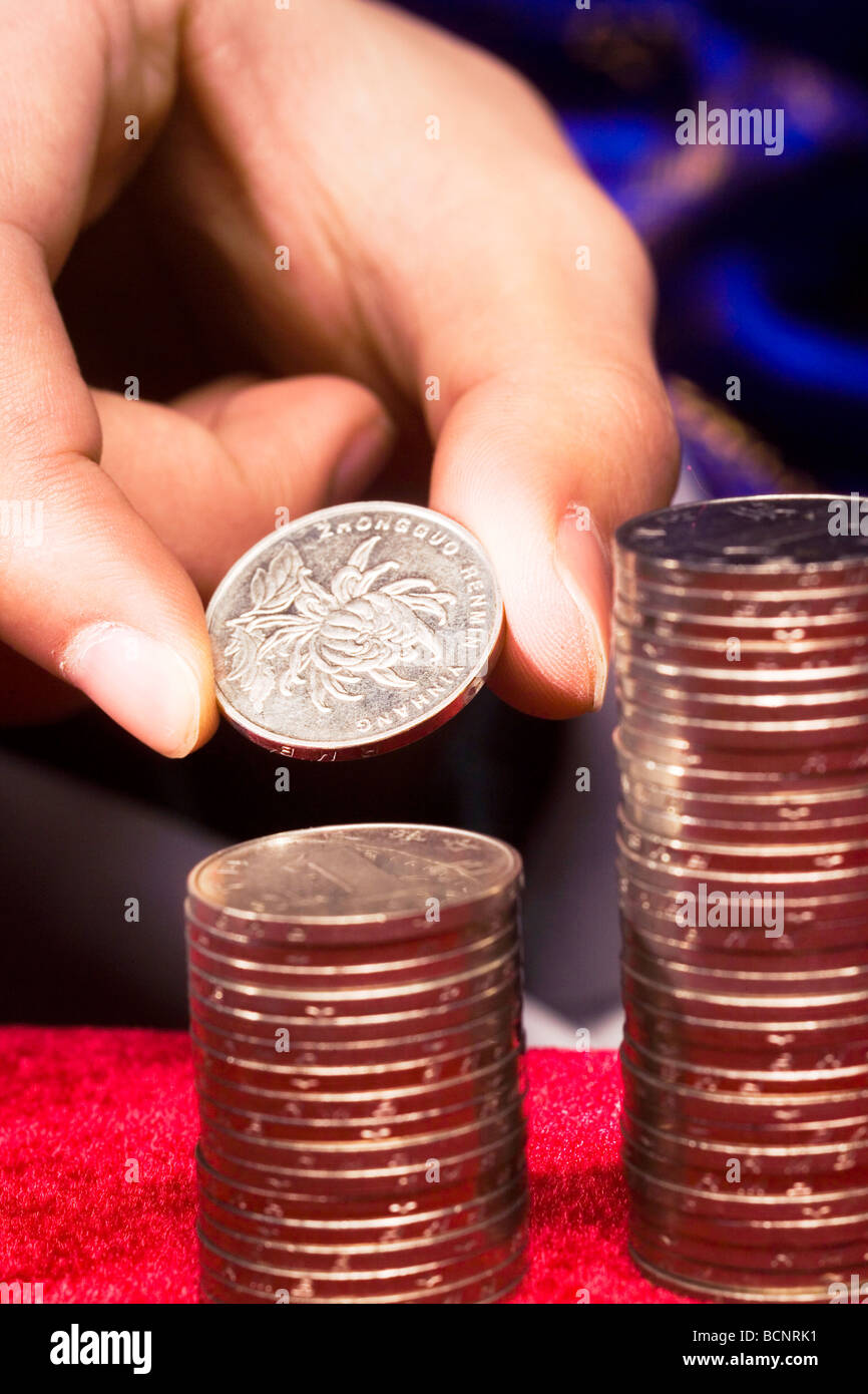 Man holding one Yuan Chinese Renminbi coin with stacks of coins Stock ...