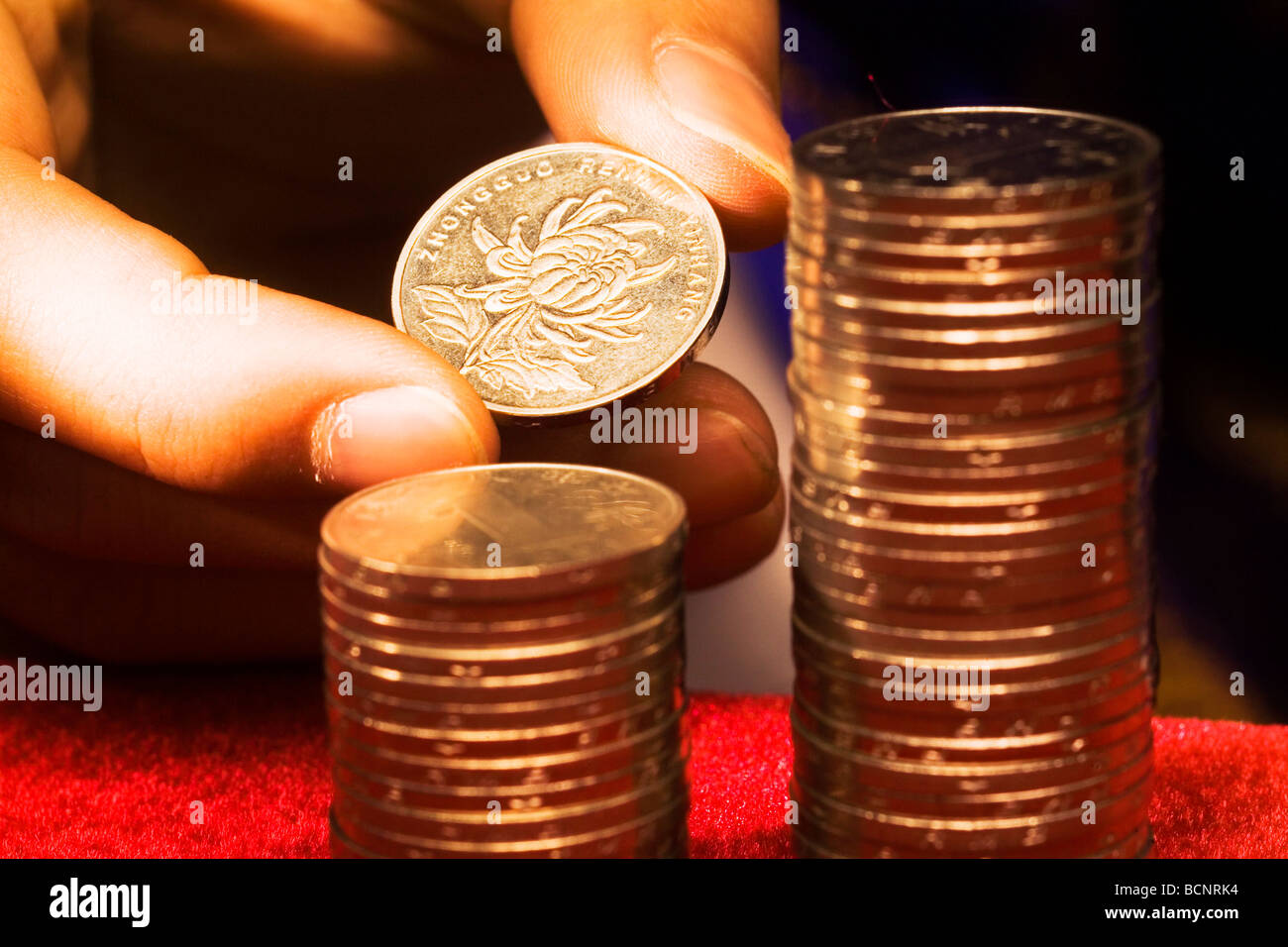 Man holding one Yuan Chinese Renminbi coin with stacks of coins Stock ...