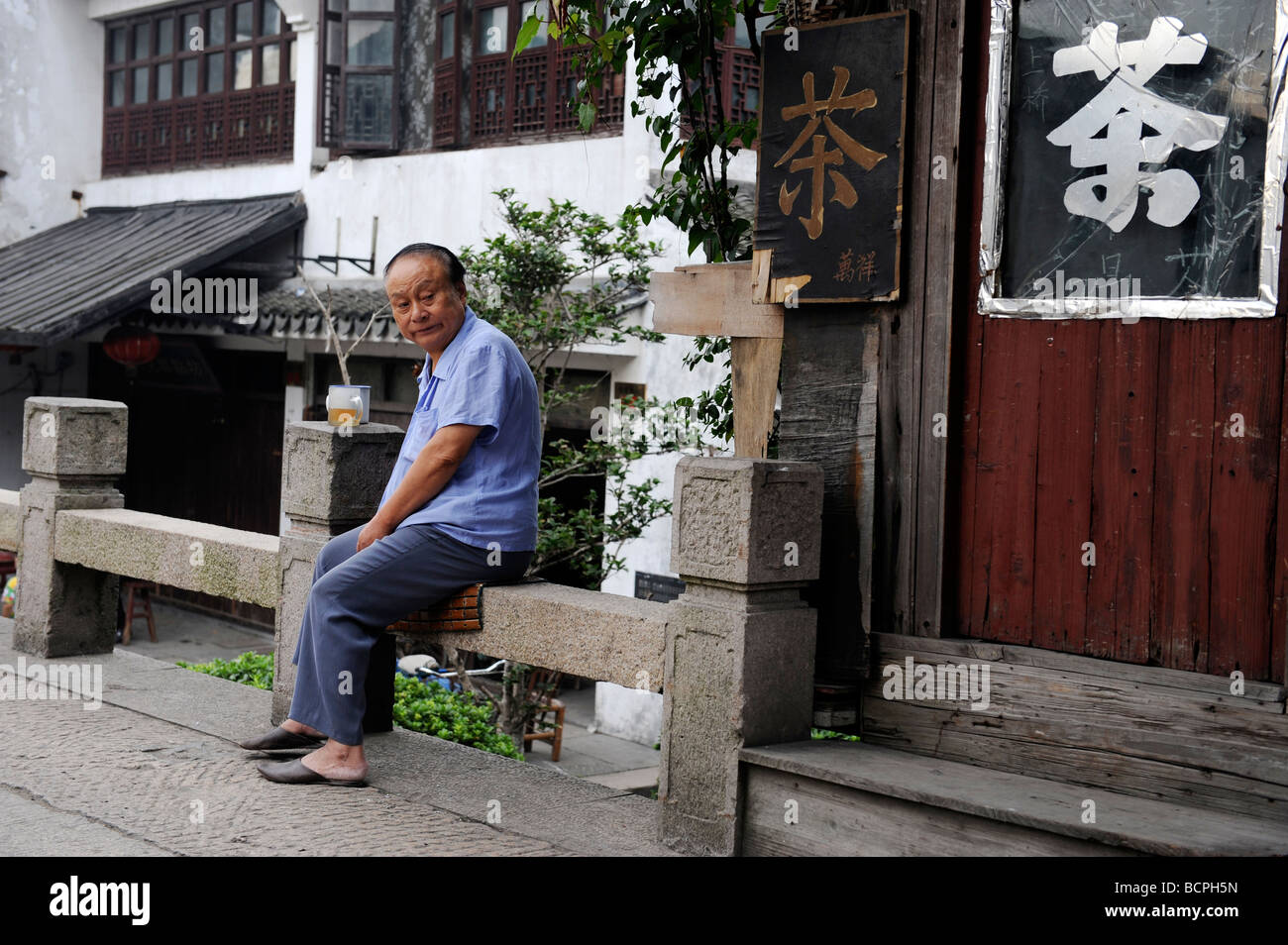 Elderly Chinese man sitting on the stone railing beside a tea house ...