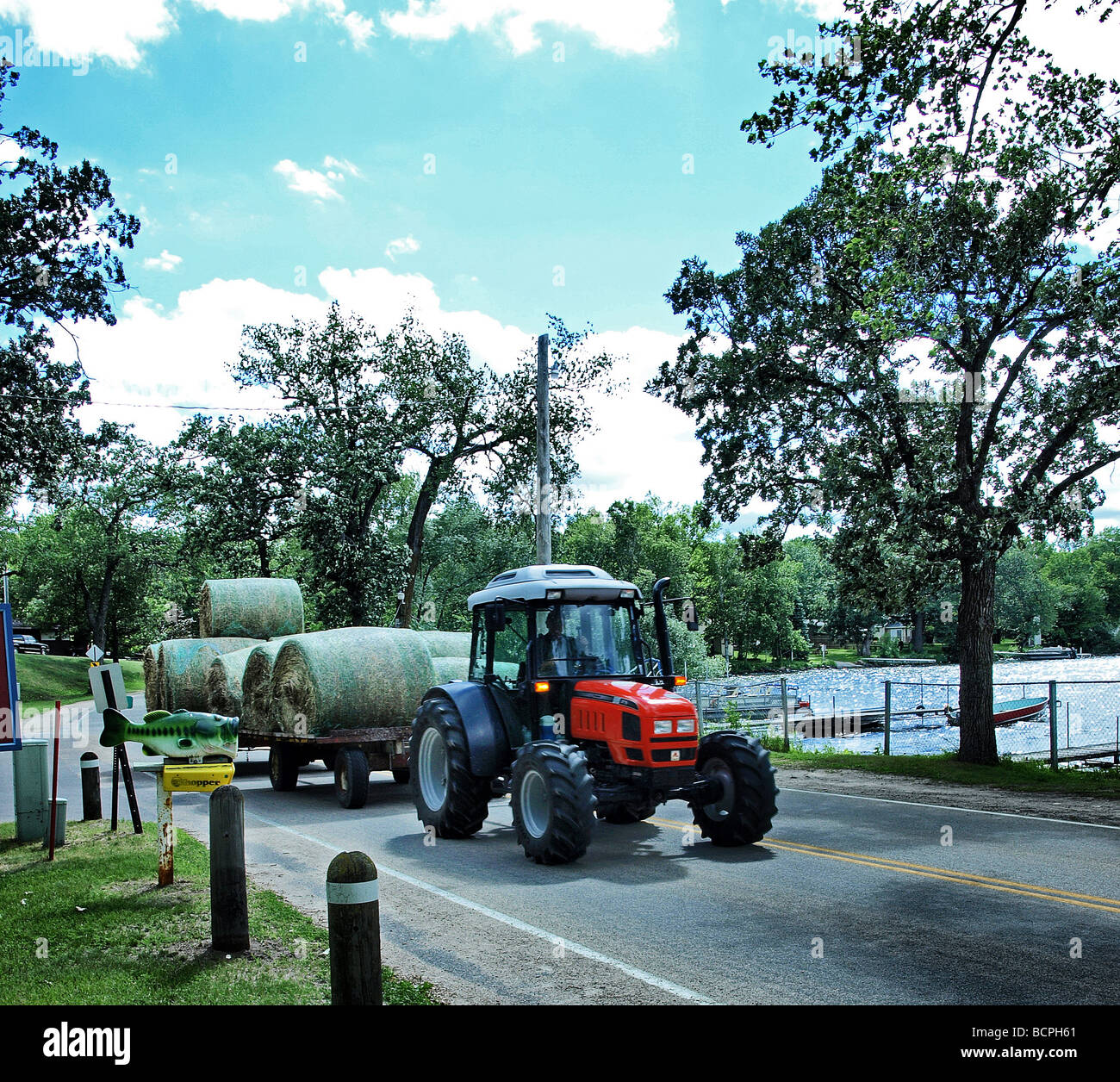 farm tractor on a road pulling rolled bales of hay with lake in ...