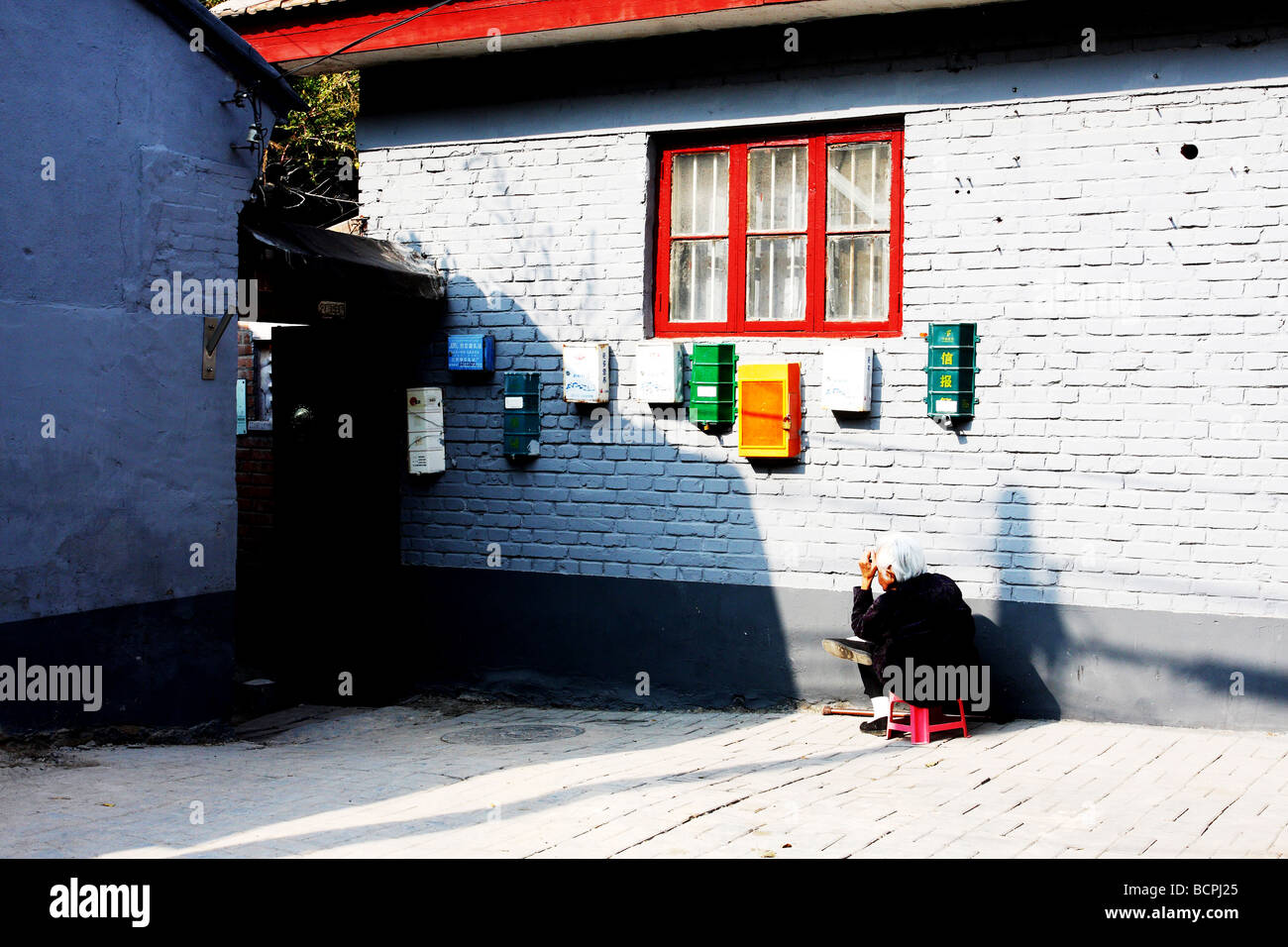 Elerly Chinese woman sitting beside a traditional courtyard house ...