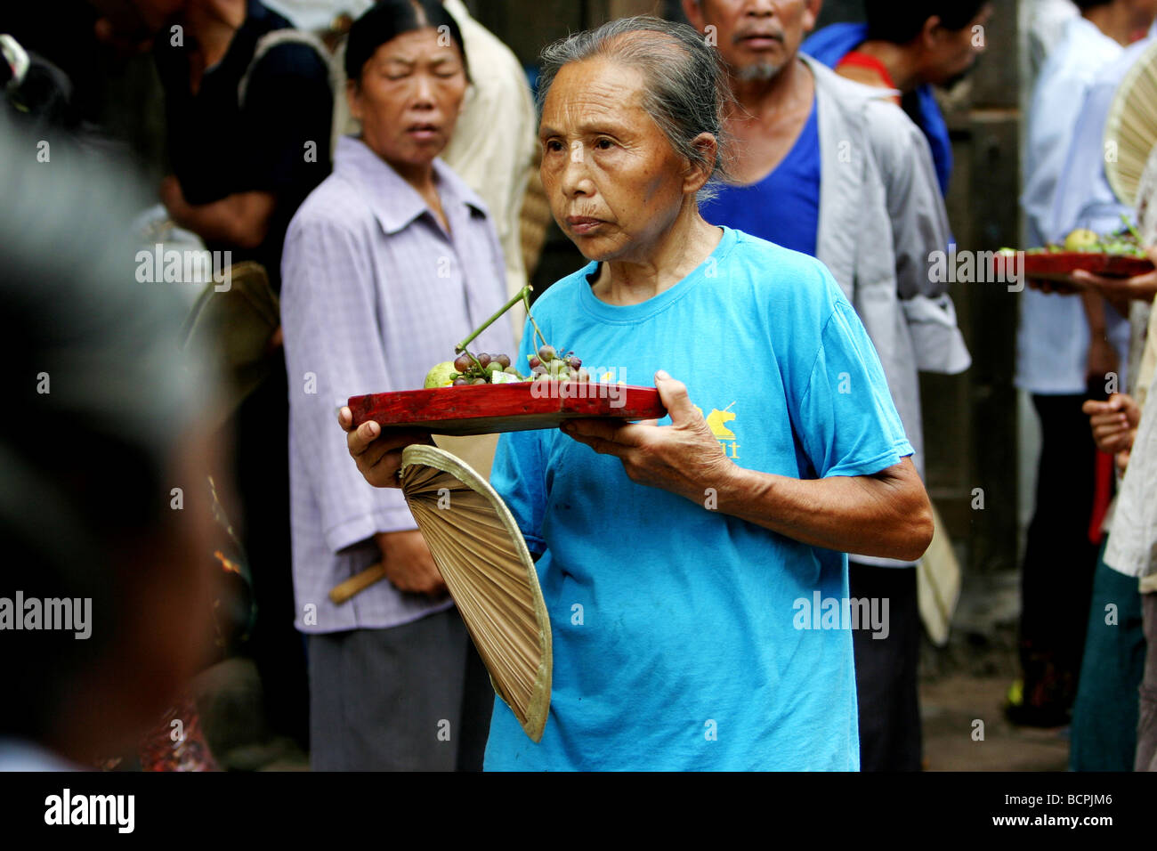 Elderly Chinese woman making offering to the shrine during temple fair ...
