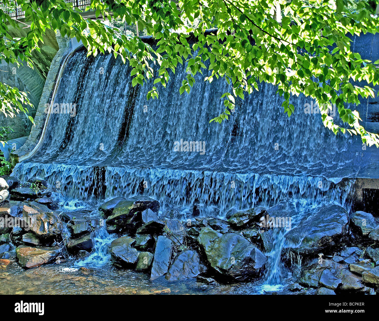 dam waterfall framed by tree branch and leaves with rocks at bottom of ...