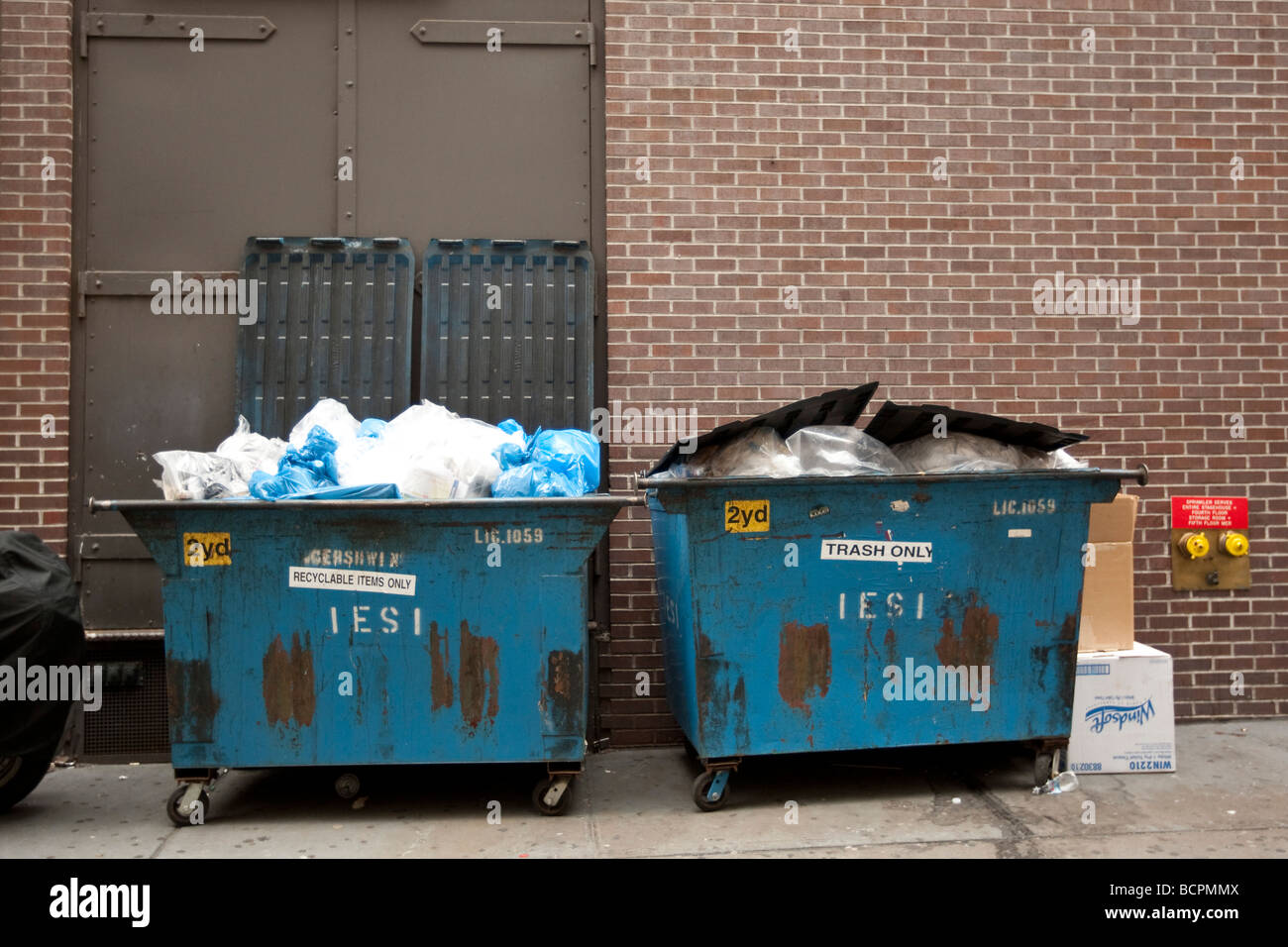 two full blue metal dumpsters against a brick wall in USA May 2009 ...