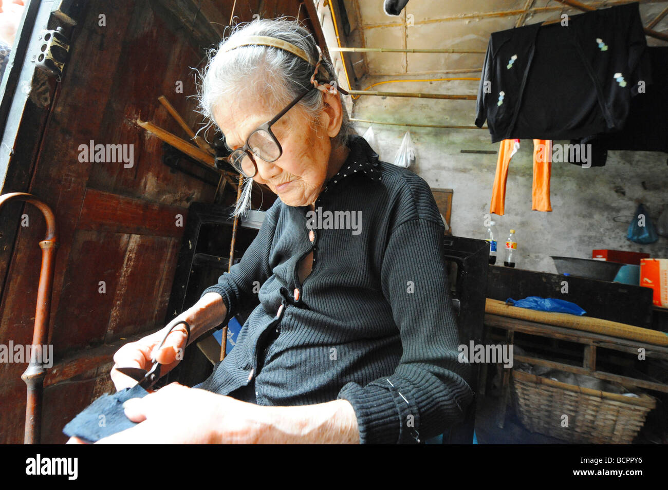 Elderly Chinese woman cutting a piece of material for sewing, Lizhuang ...