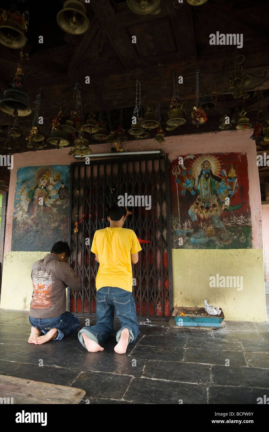 Two young Hindu men worship / pray at the altar shrine locked door of ...