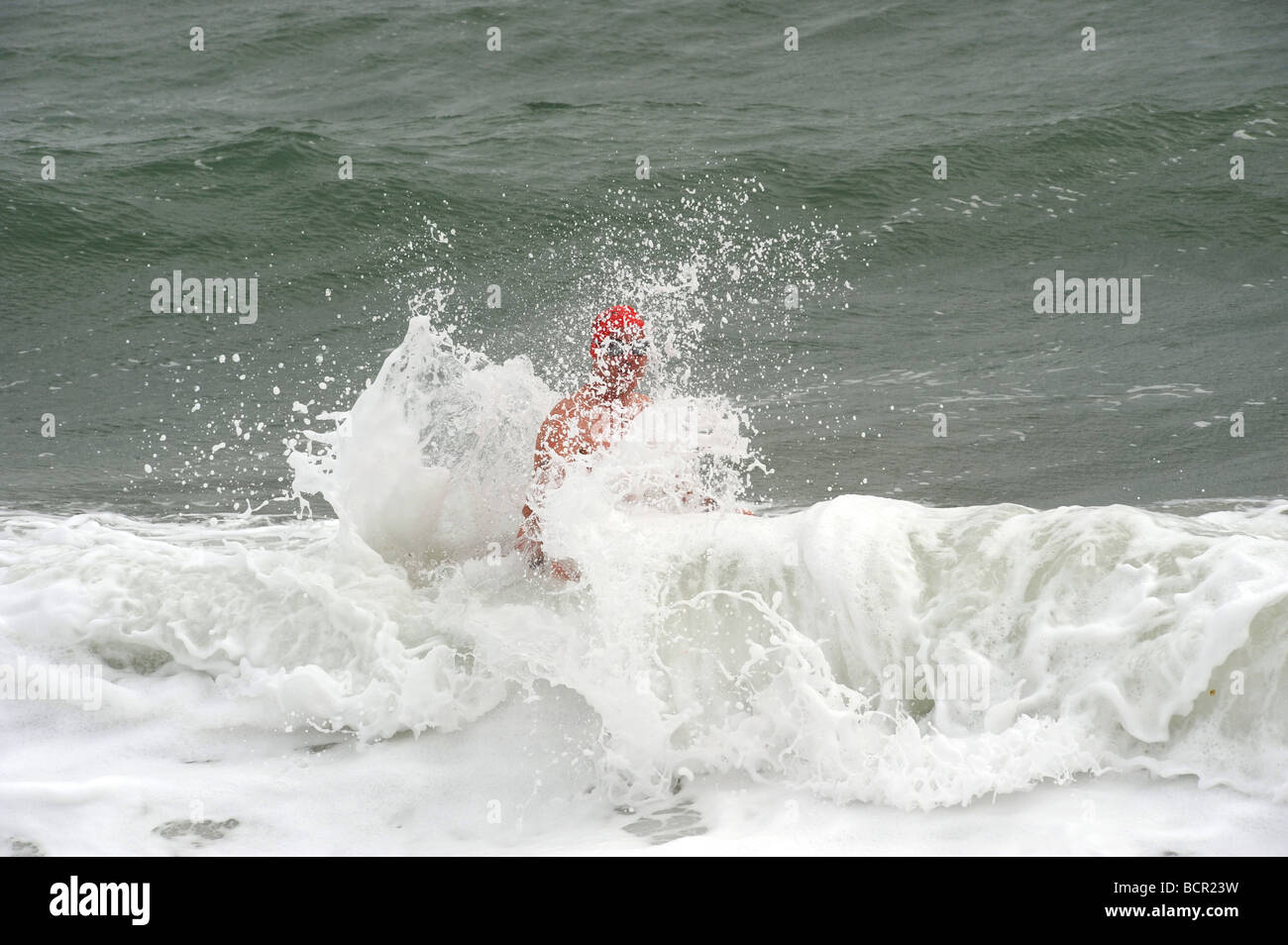 A man gets engulfed by a wave as he prepares to go swimming in a choppy ...