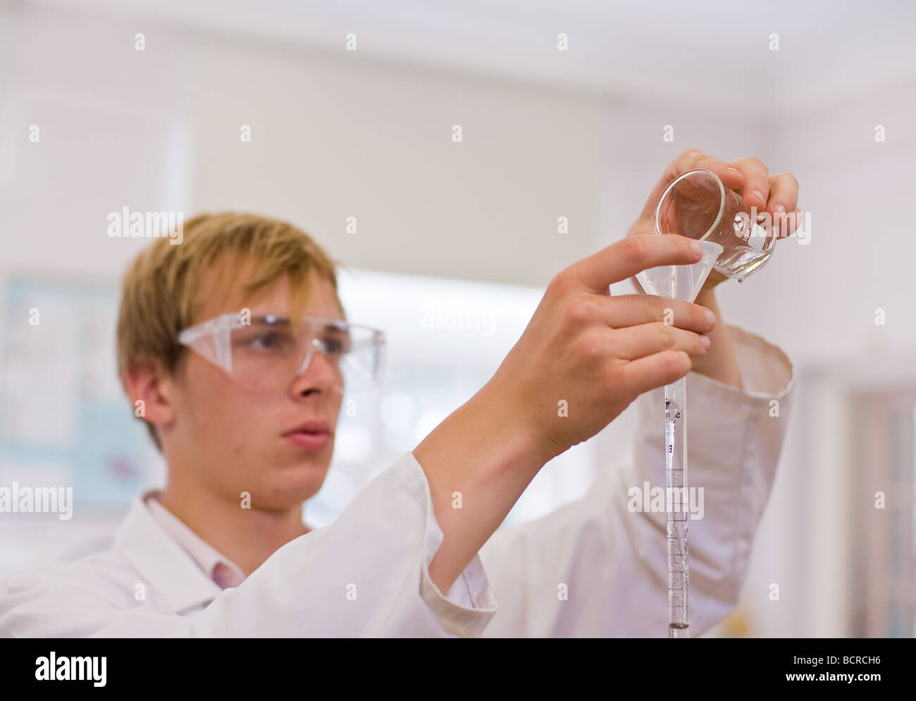 A student pouring liquid into a funnel in a school science laboratory ...