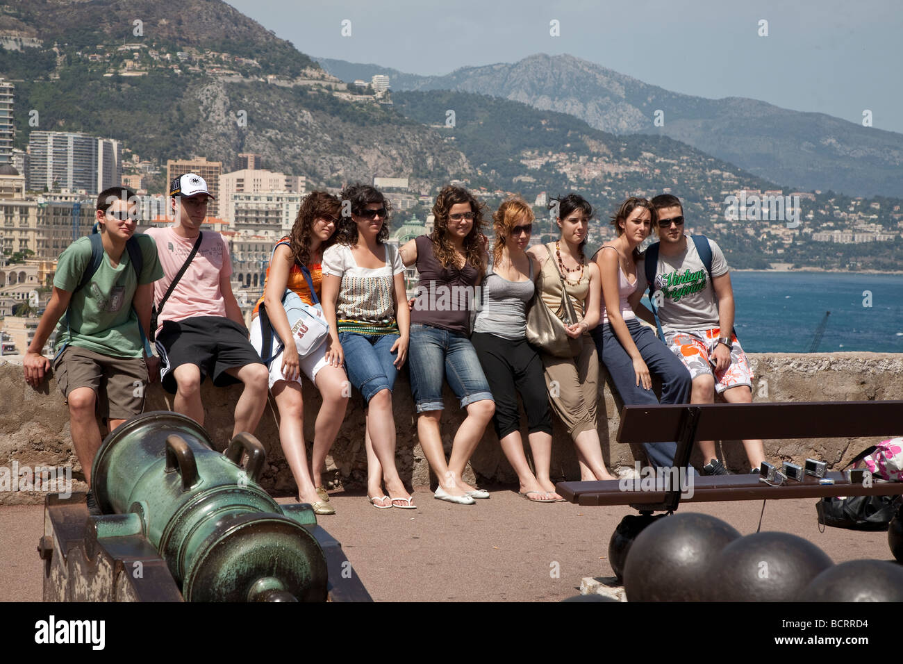 Group of young people sitting on wall of Palace of Monaco in summer ...