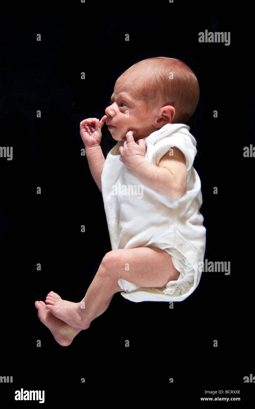 Newborn baby boy picking his nose photographed on a black studio ...