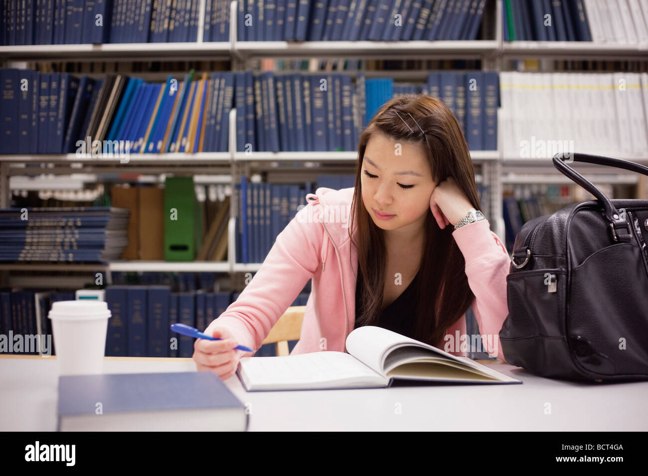 Asian girl in the library studying from a textbook Stock Photo - Alamy