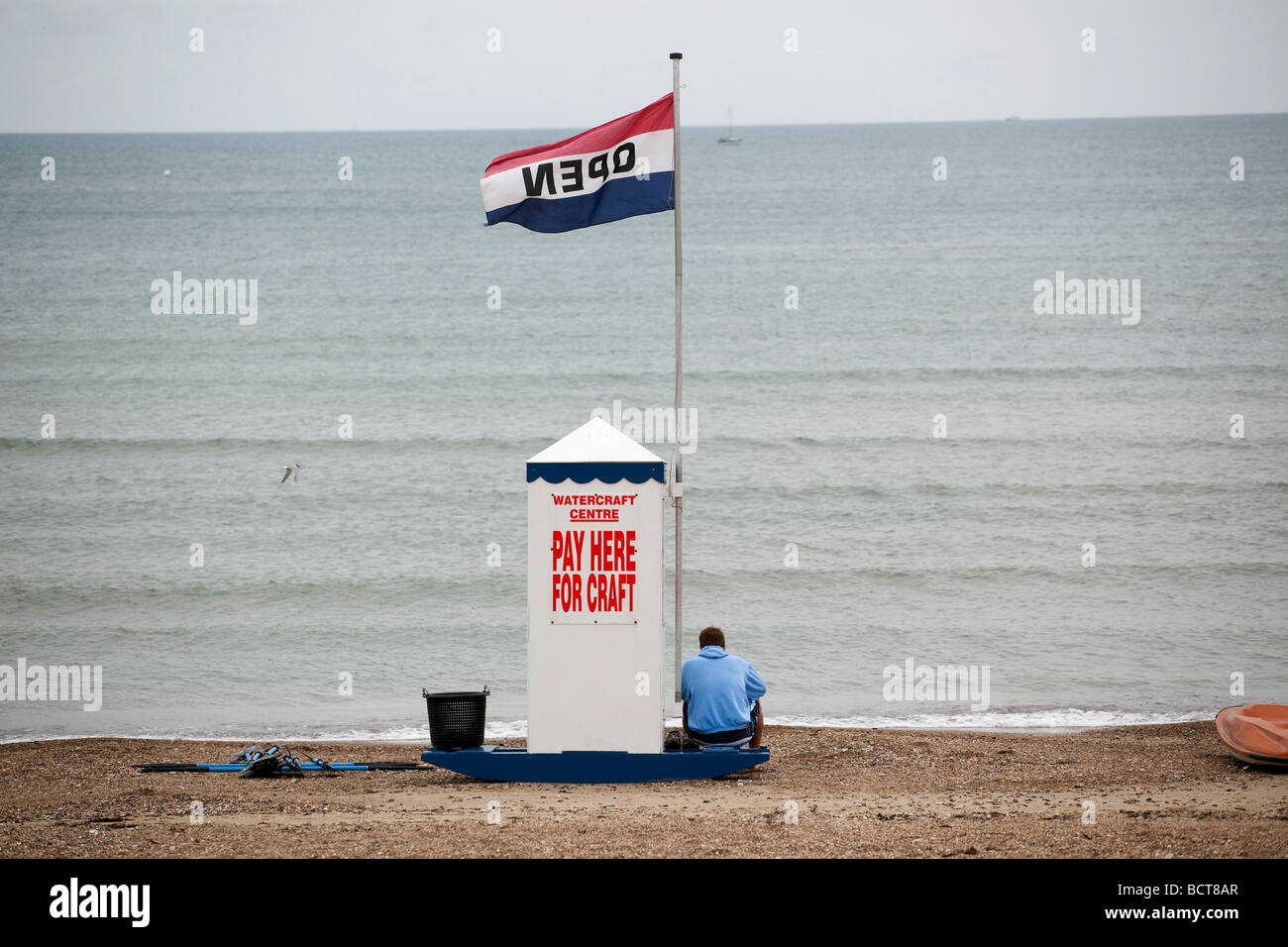 A beach trader sits alone on an empty beach awaiting customers to rent ...