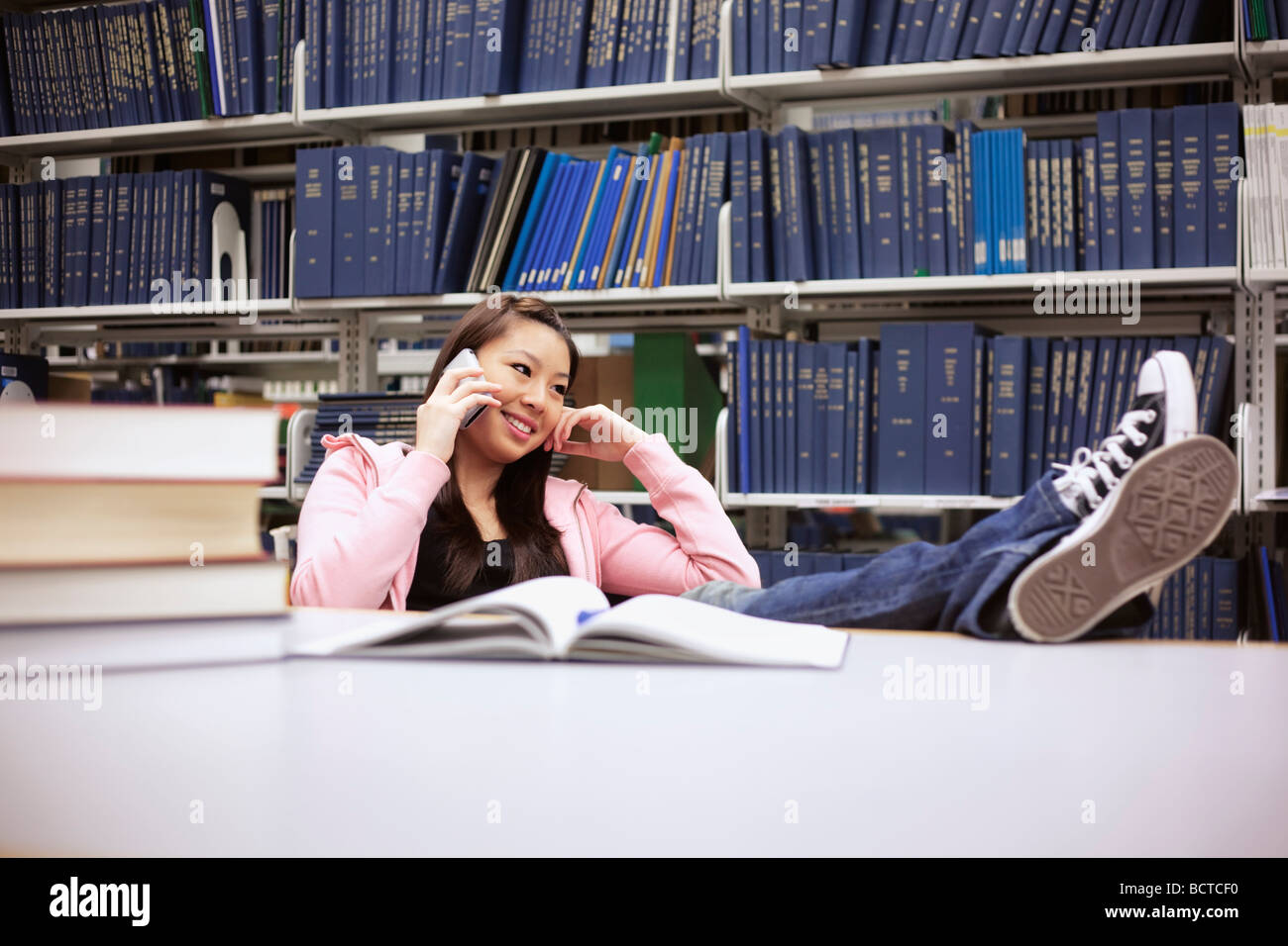 An Asian girl sitting in the library with her feet on a table while she ...