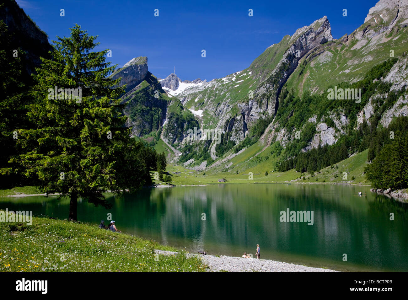 People resting on the shore of the emerald Seealpsee mountain lake ...