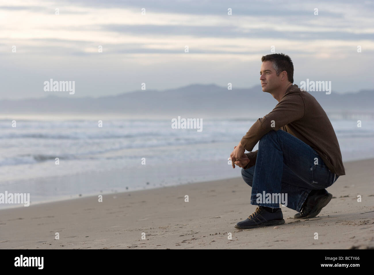 Side profile of a mid adult man crouching on the beach Stock Photo - Alamy