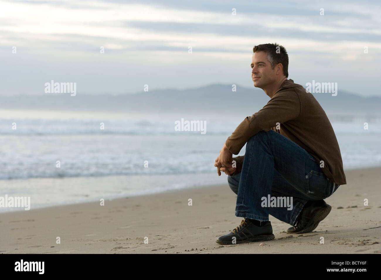 Side profile of a mid adult man crouching on the beach Stock Photo - Alamy