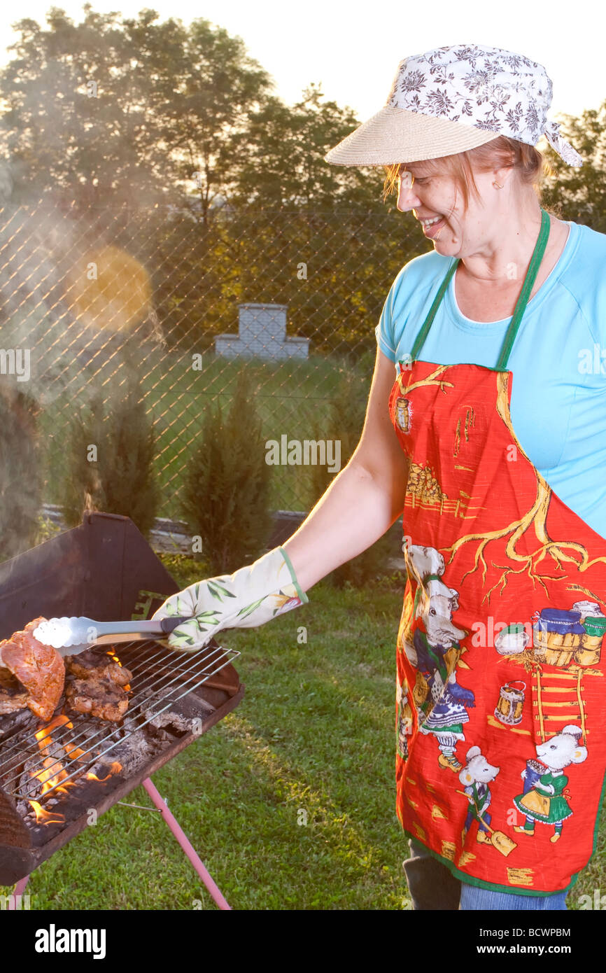 Woman holding barbecuing pork on grill with tongs Stock Photo - Alamy