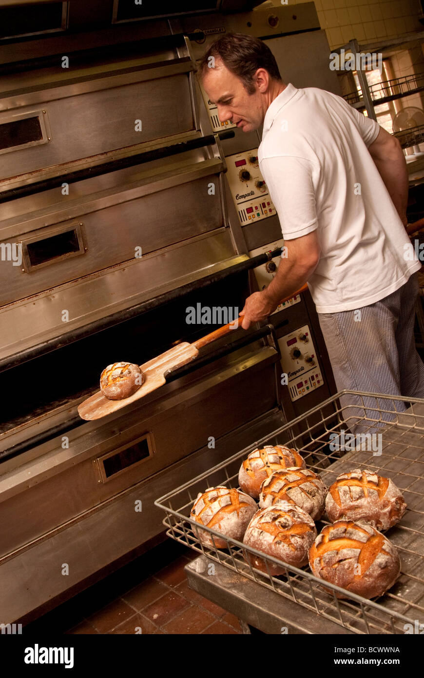 baker taking a loaf of bread from the oven with a wooden paddle Stock ...