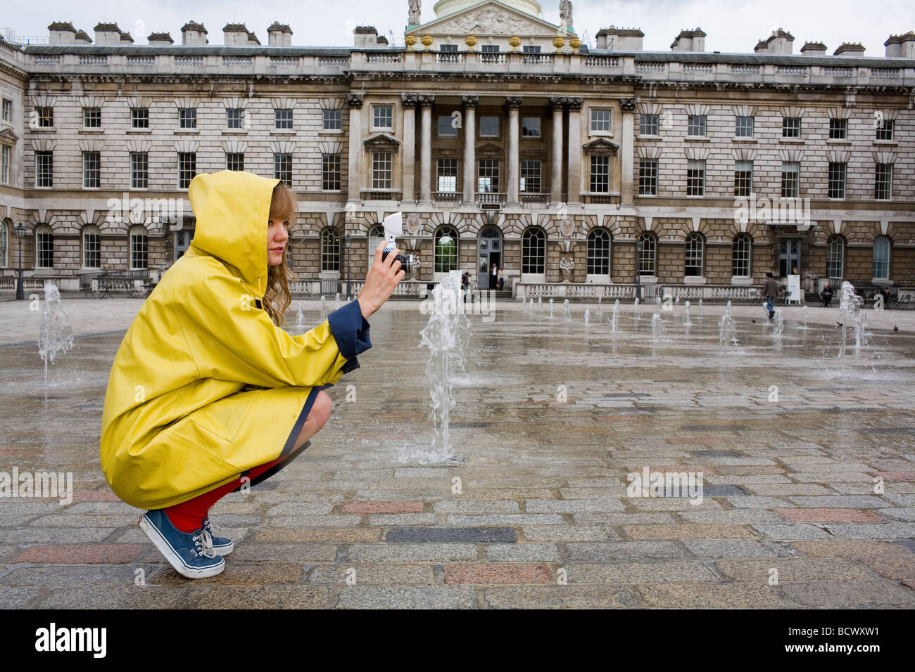 A young woman in yellow waterproof mac coat red socks and blue shoes ...