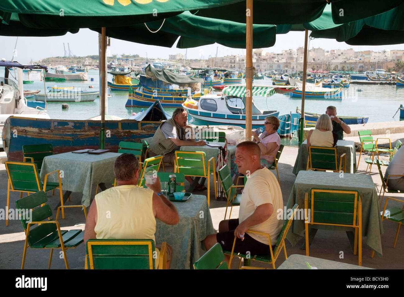 tourists drinking at a bar in the fishing harbour of Marsaxlokk, Malta ...