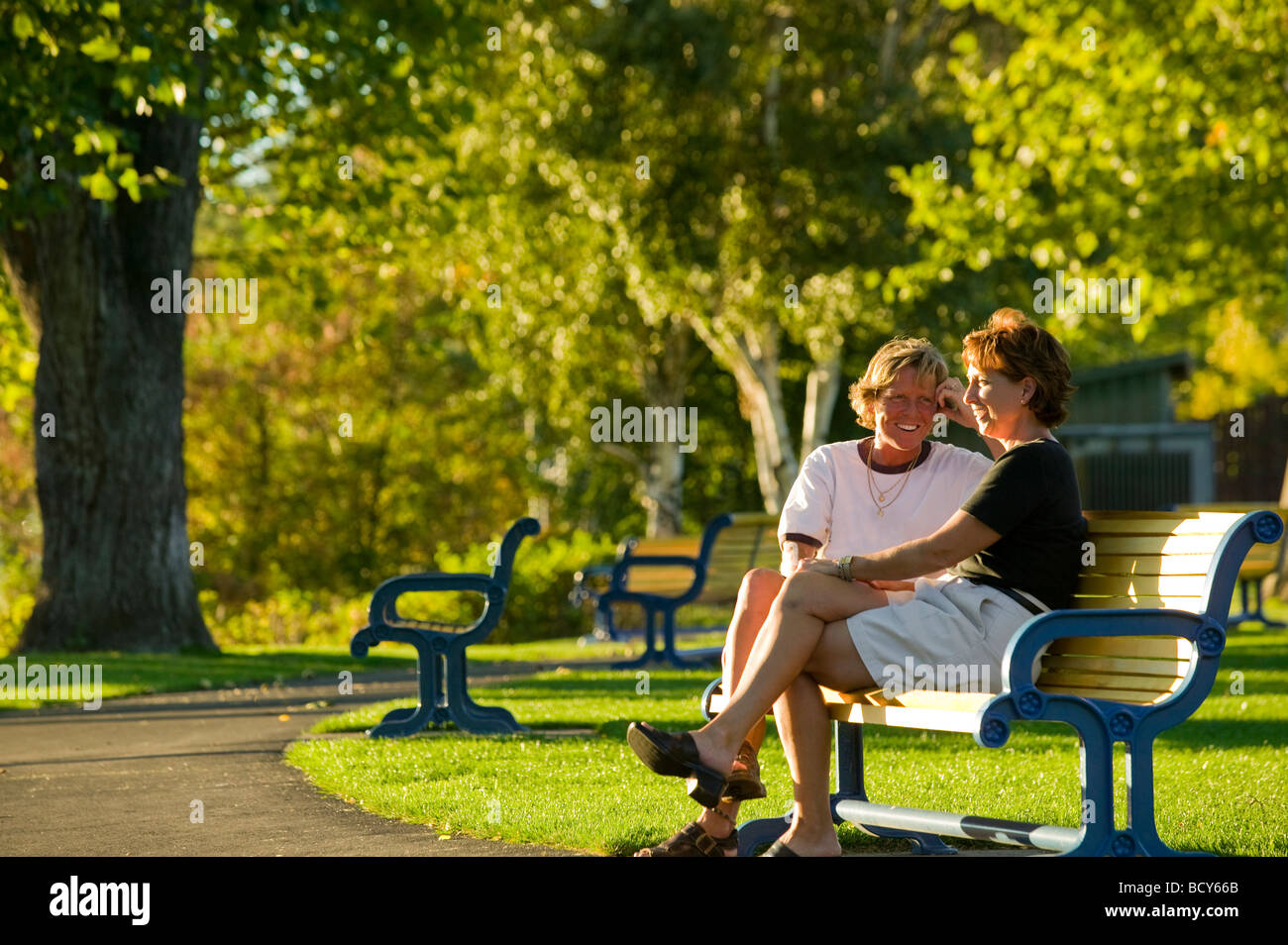 Two mature women sitting on park bench talking Stock Photo - Alamy