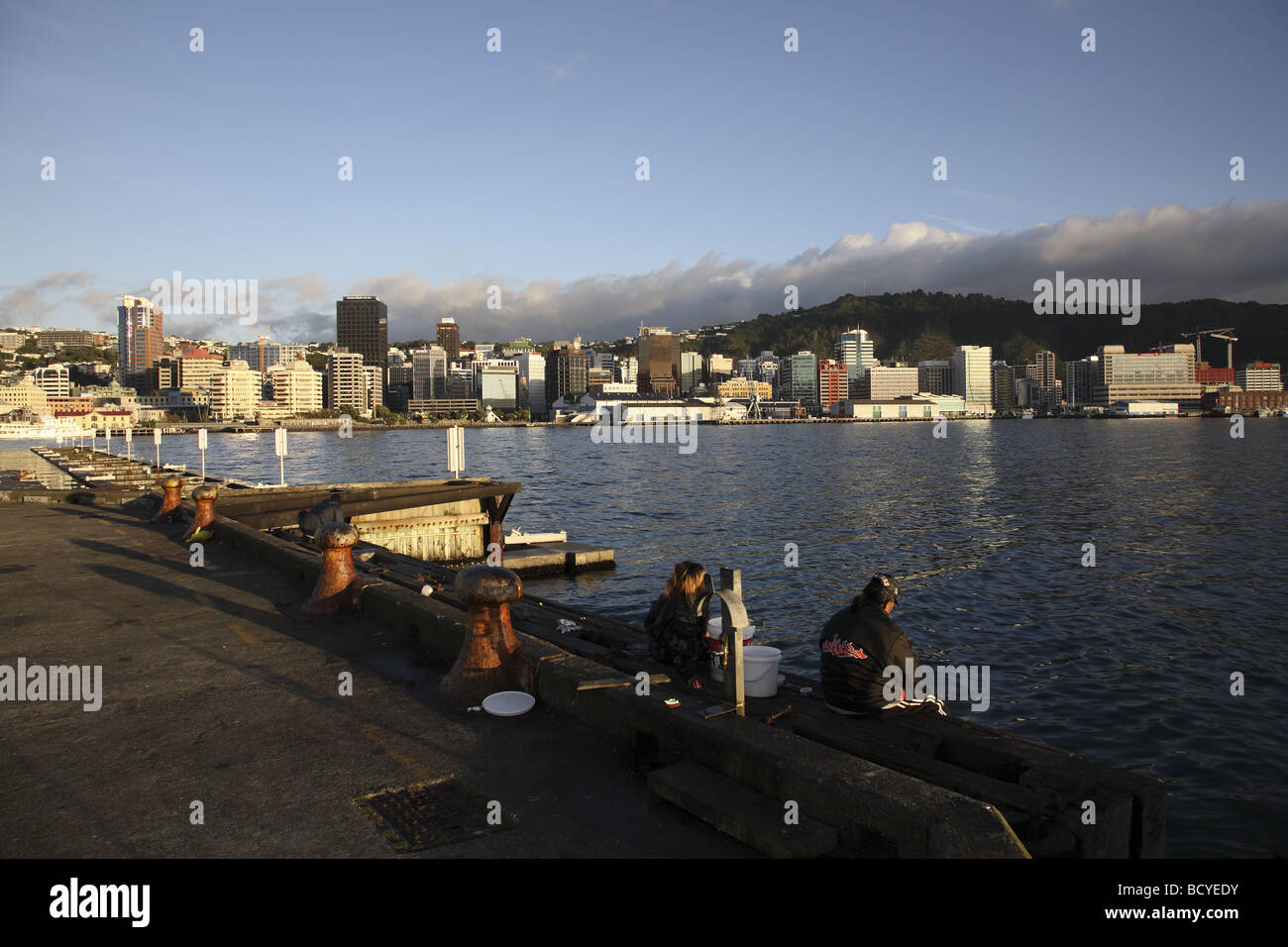 People fishing on the wharf with Wellington cityscape behind ...