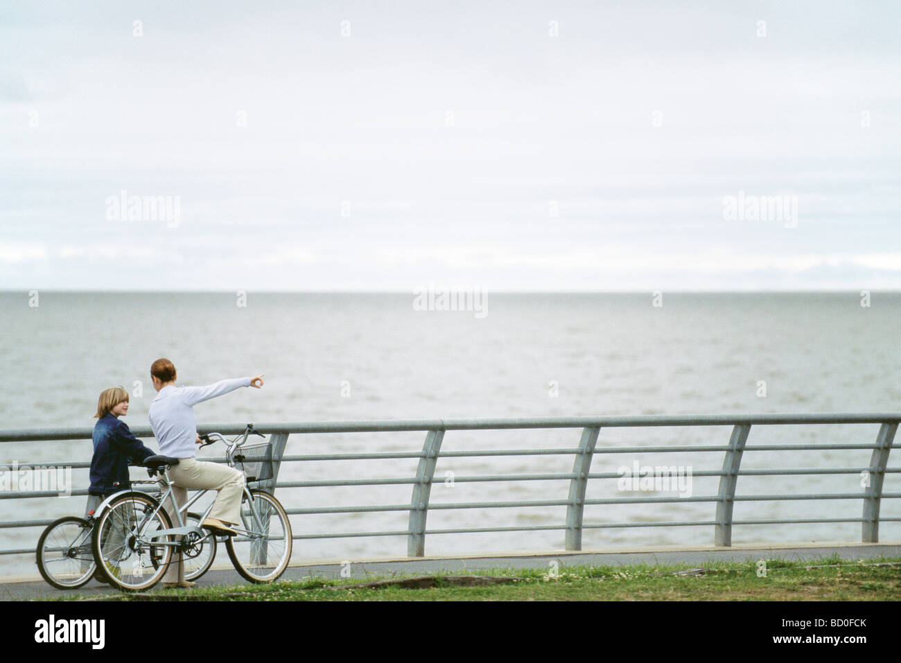 Mother and son on bicycle outing at seaside park, mother pointing to ...