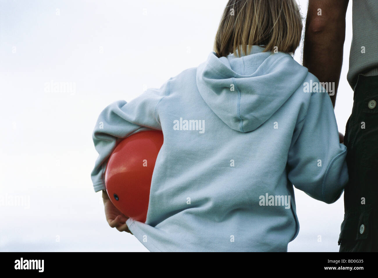 Young boy holding father's hand, carrying ball under arm, rear view ...