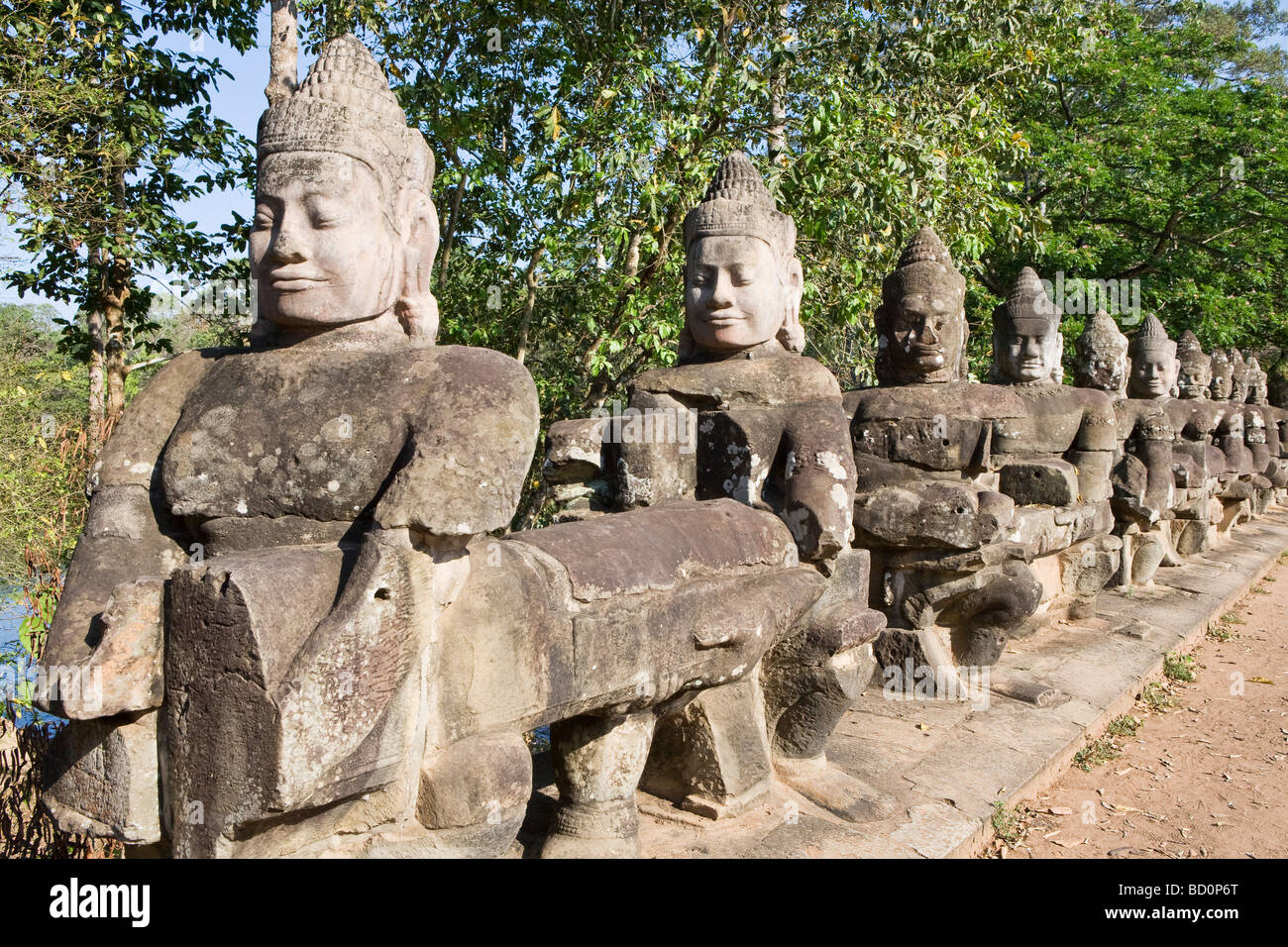 A line of stone statues leading up to a gateway to Angkor Thom in ...