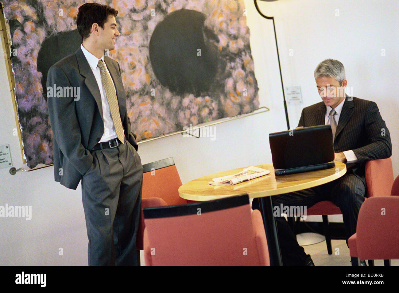 Businessmen chatting in break room, one using laptop computer Stock ...