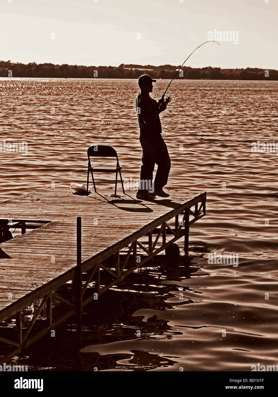 solo fisherman fishing on a dock that projects into a lake all in sepia ...