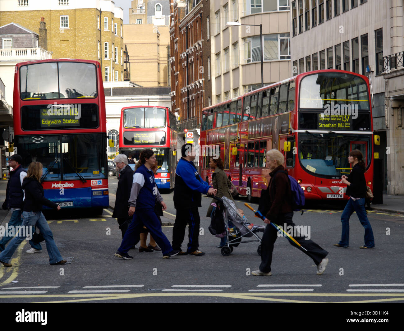 People crossing the street with red London buses in the background ...