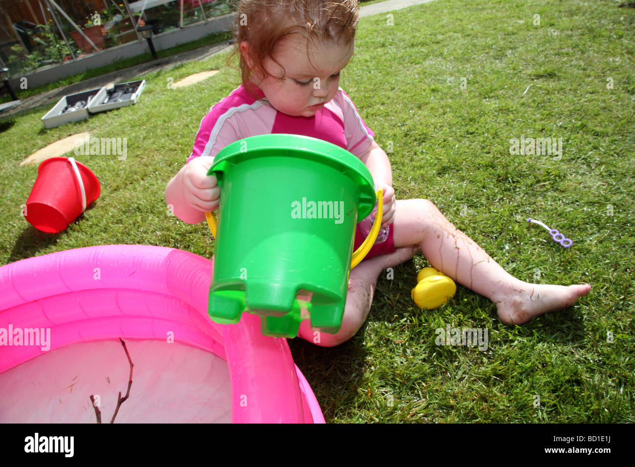 Female child playing with a bucket in a garden on a summer afternoon in ...