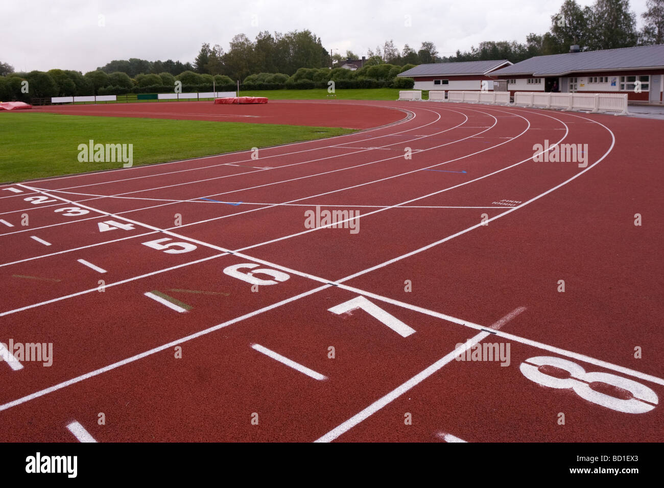 Red racetrack of stadium with soft covering near houses and wood Stock ...