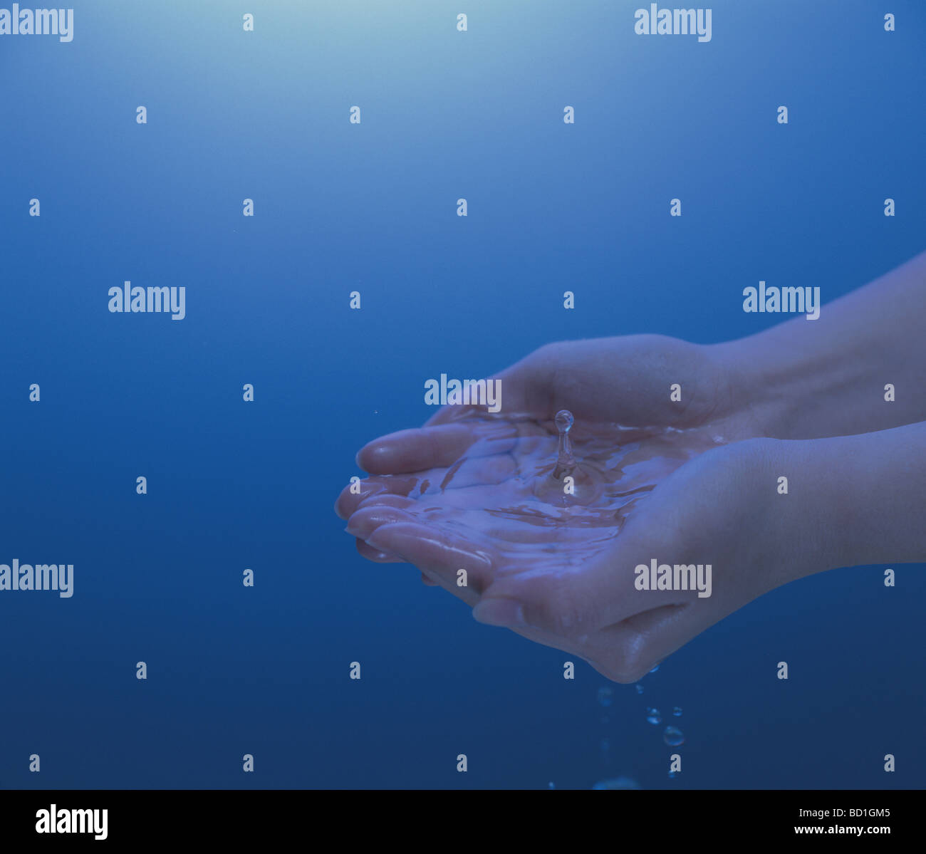 Woman holding water in hands blue background Stock Photo - Alamy