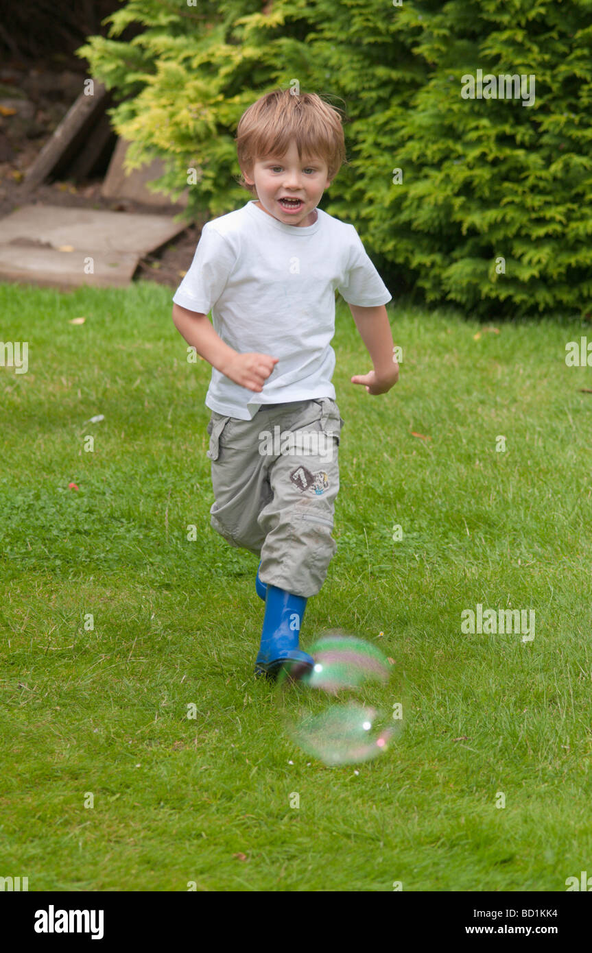 little boy chasing bubbles in garden, running and having fun, three ...