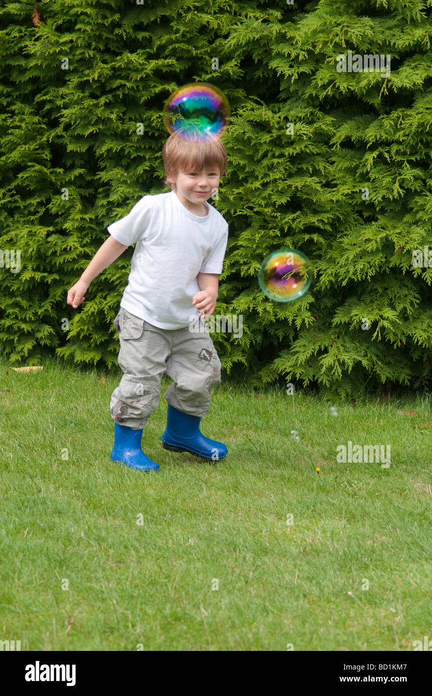 little boy chasing bubbles in garden, running and having fun, three ...