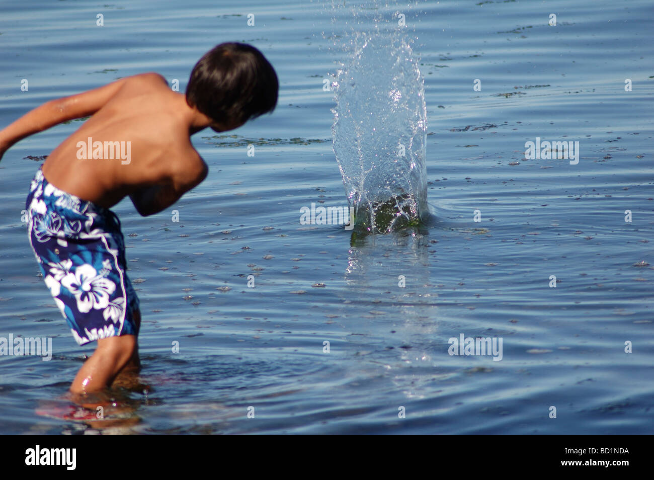 Young boy tossing a stone in the water and making the water splash ...