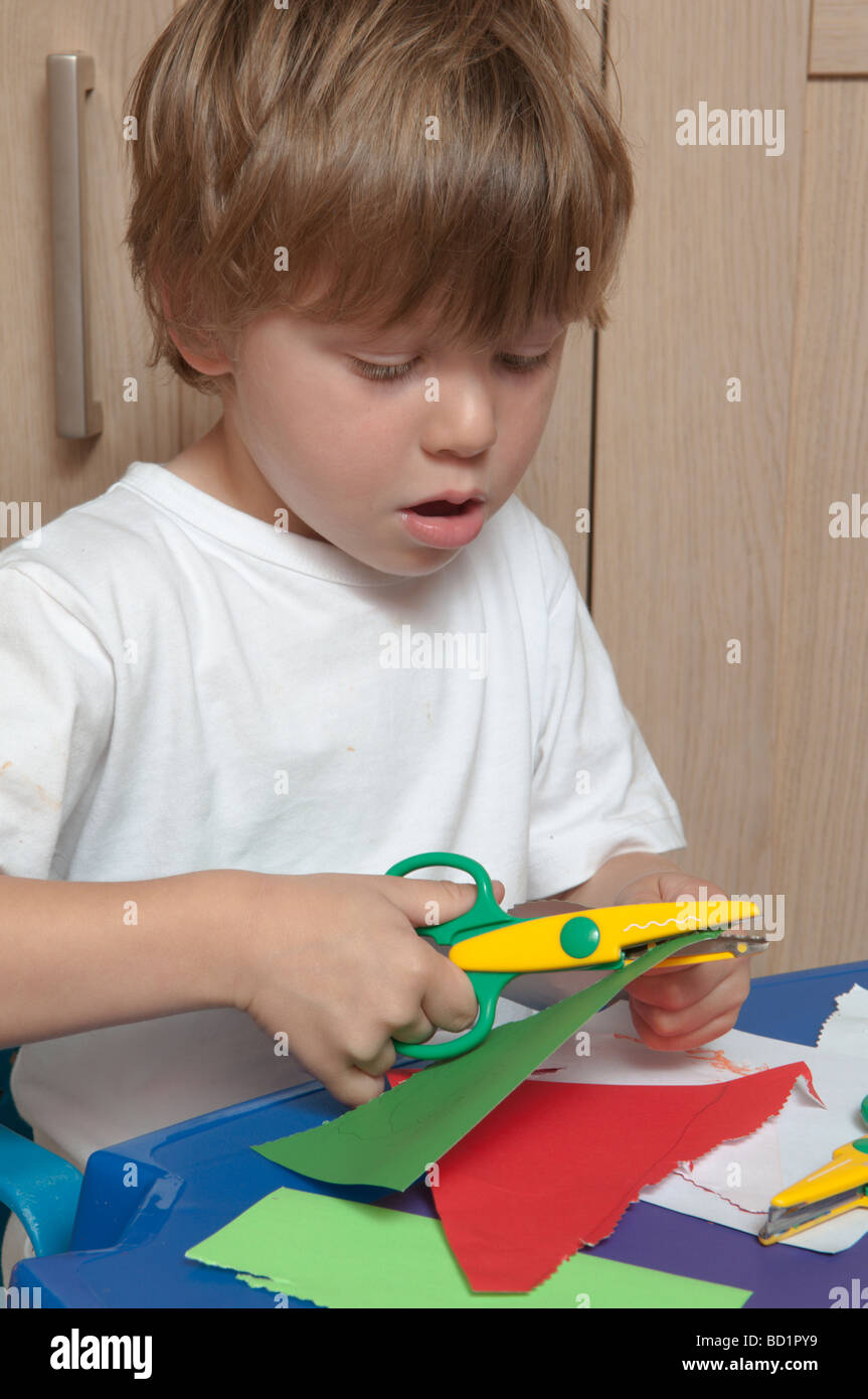 young boy cutting modelling paper with small scissors sitting at small ...