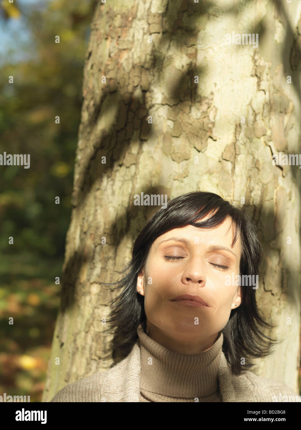 Woman leaning against tree in sunshine Stock Photo - Alamy