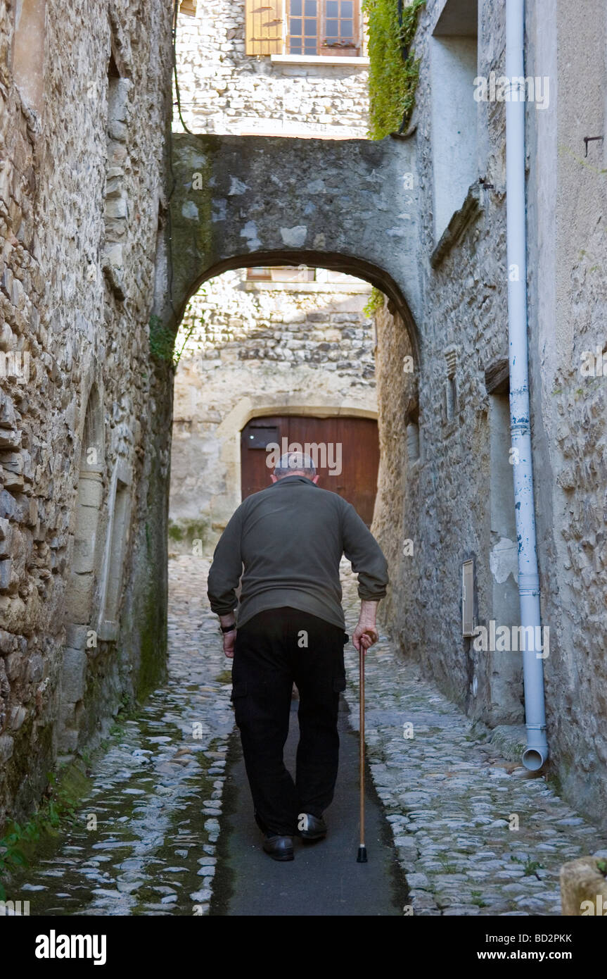 Rear view of an old Frenchman with a walking stick along a cobbled path ...