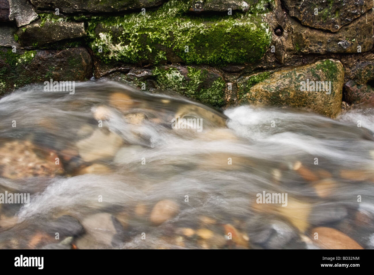 Photograph of fast moving water flowing against a wall over rocks and ...