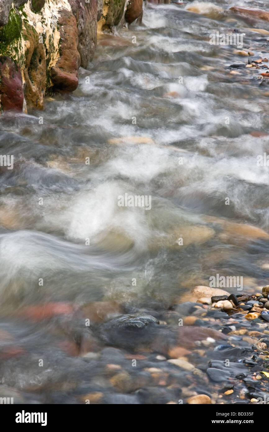Photograph of fast moving water flowing against a wall over rocks and ...