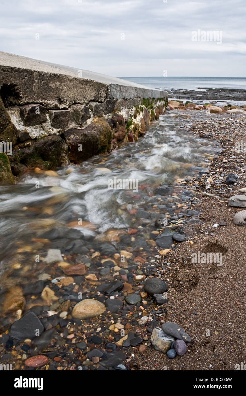 Photograph of fast moving water flowing against a wall over rocks and ...