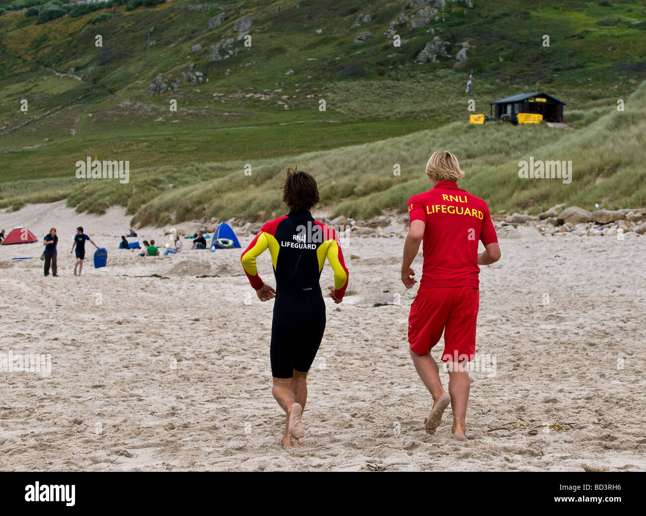 Two RNLI lifeguards running on Sennen beach in Cornwall Stock Photo - Alamy