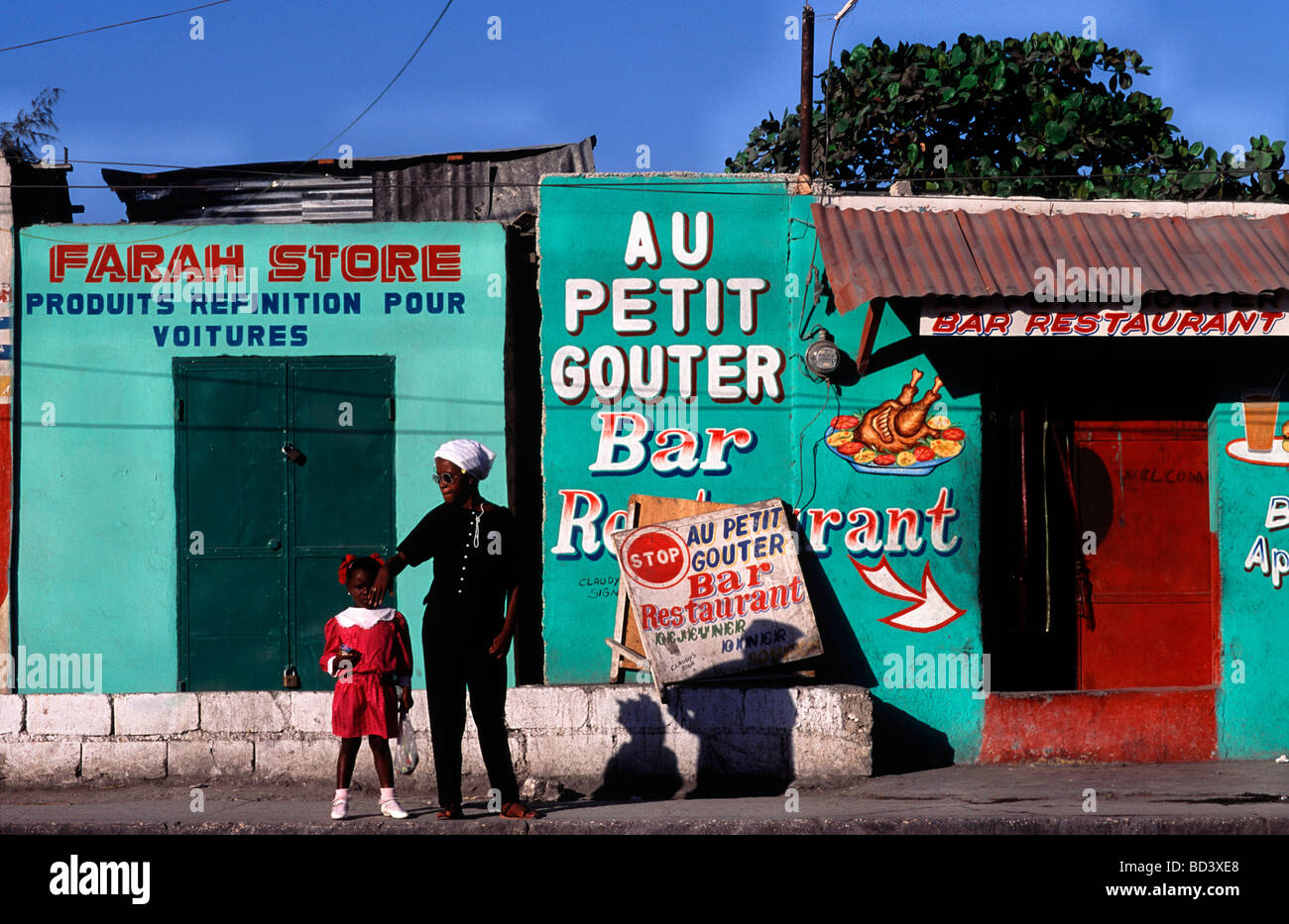 Haitian woman and young child in front of a store and bar and ...